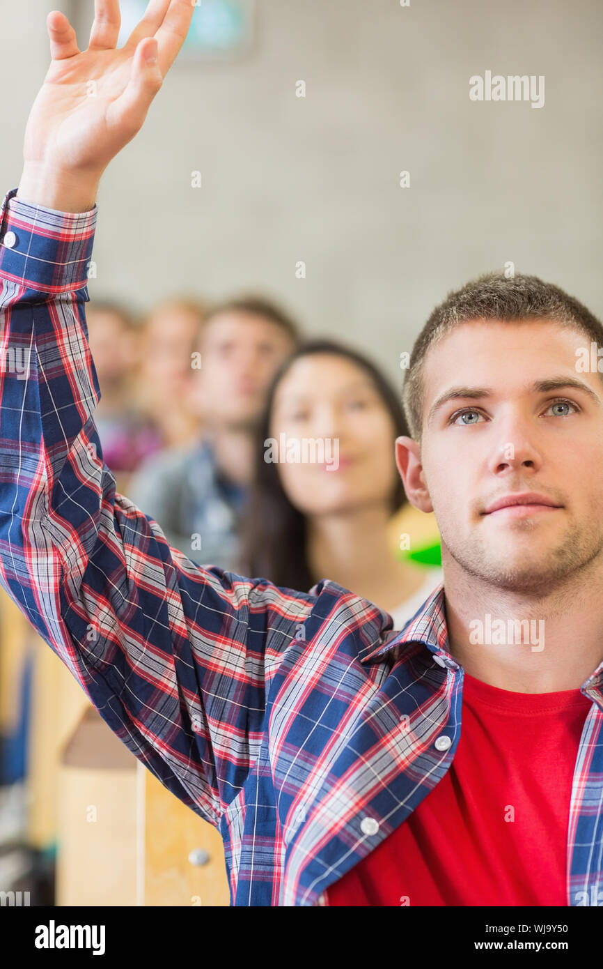 Close-up of a young male student raising hand by others in a row at the ...