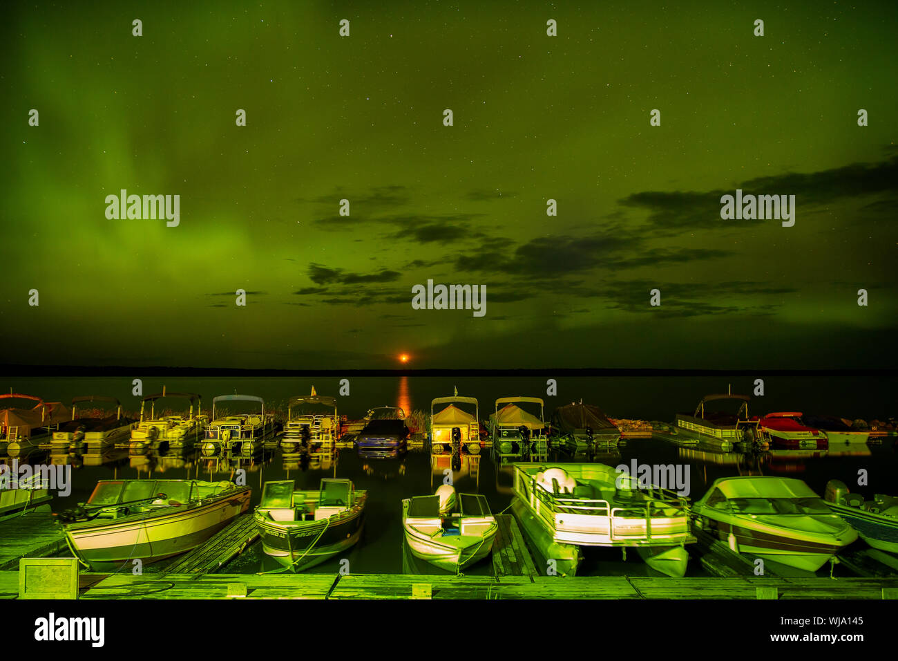 Bright green aurora borealis over a boat dock at a lake in a canadian ...