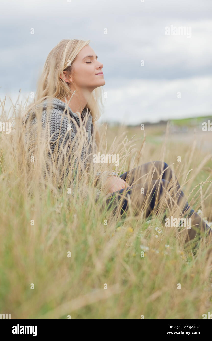 Side View Of A Cute Thoughtful Young Woman Sitting On Grass At Beach