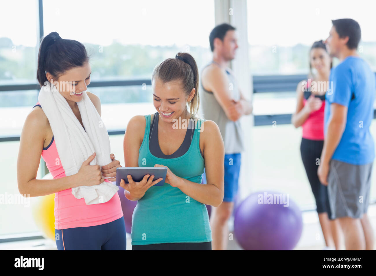 Fit women looking at digital table with friends chatting in background ...
