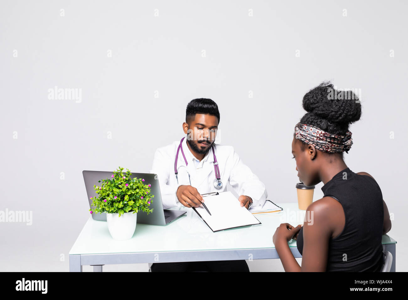 patient sitting with doctor behind wooden table and signing document ...