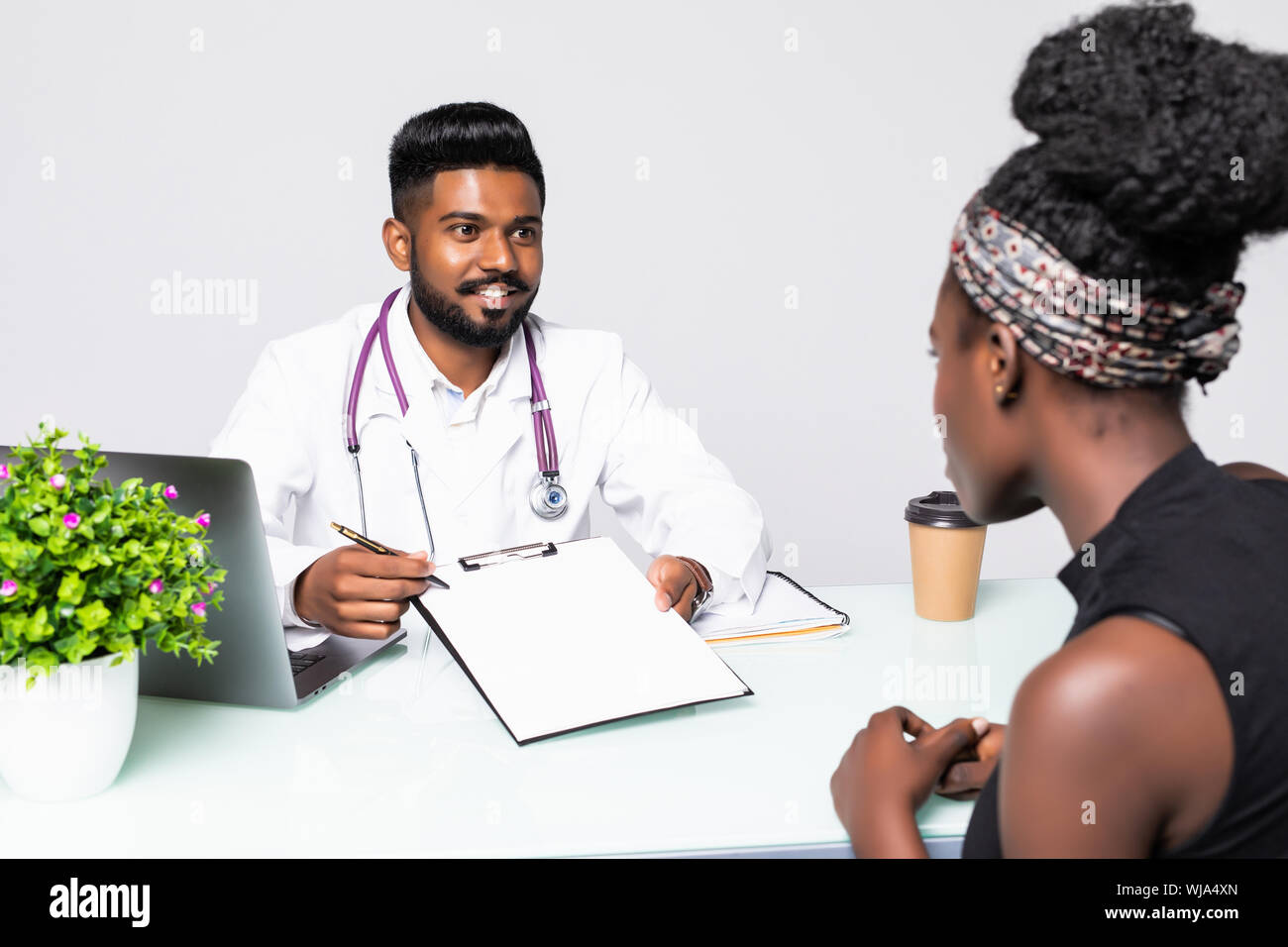 patient sitting with doctor behind wooden table and signing document ...