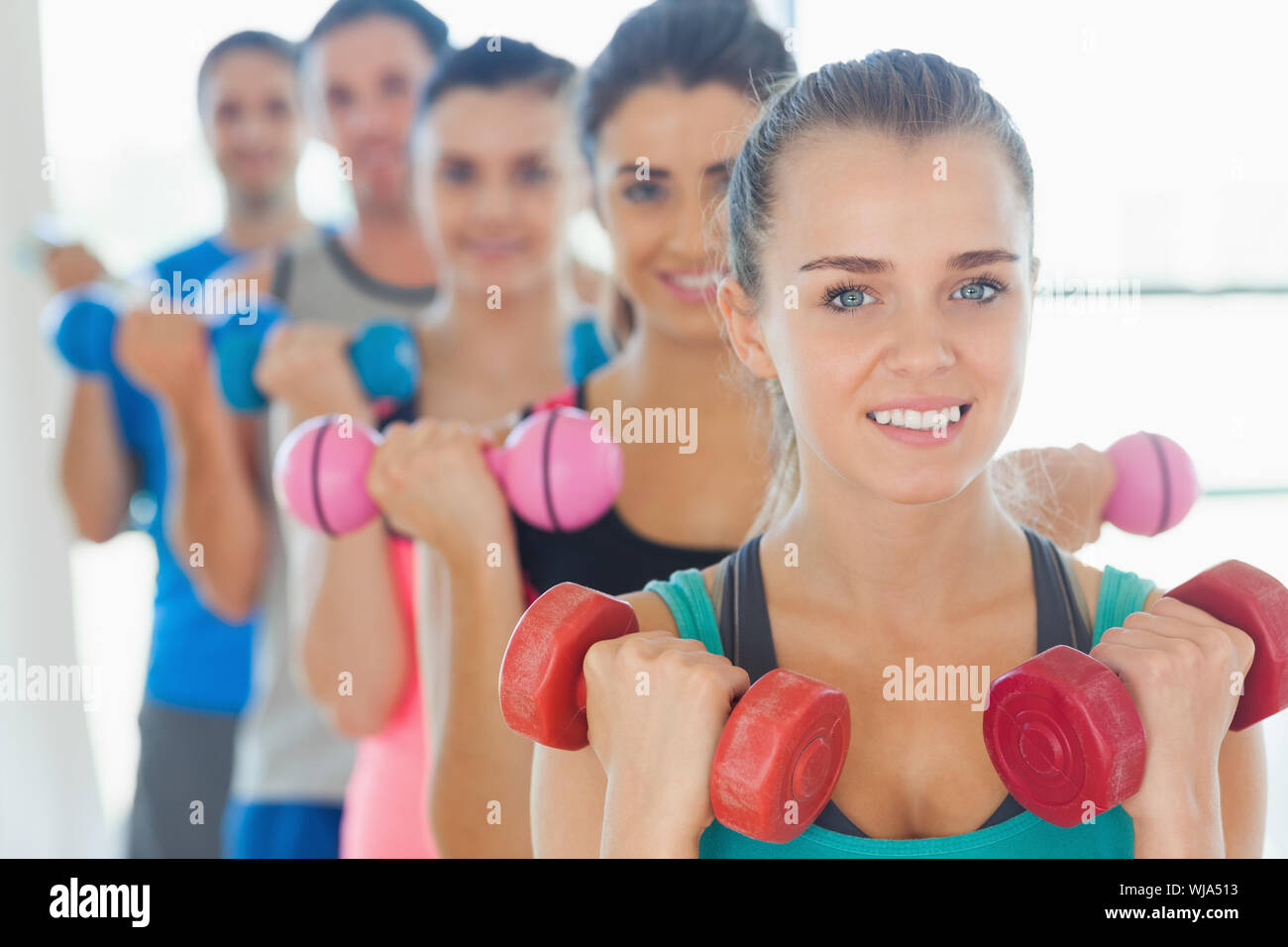 Portrait of young people lifting dumbbell weights with trainer in a ...