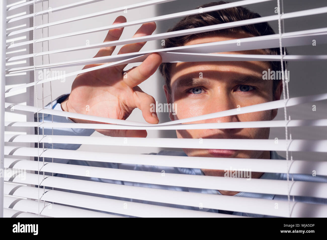 Close up portrait of a young businessman peeking through blinds Stock ...