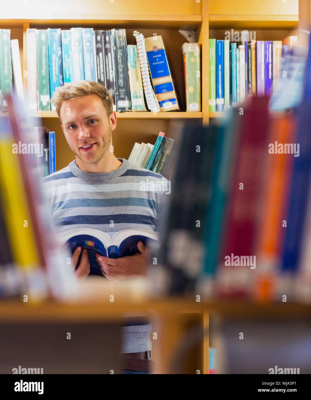 Portrait of a young male student reading a book amid bookshelves in the ...