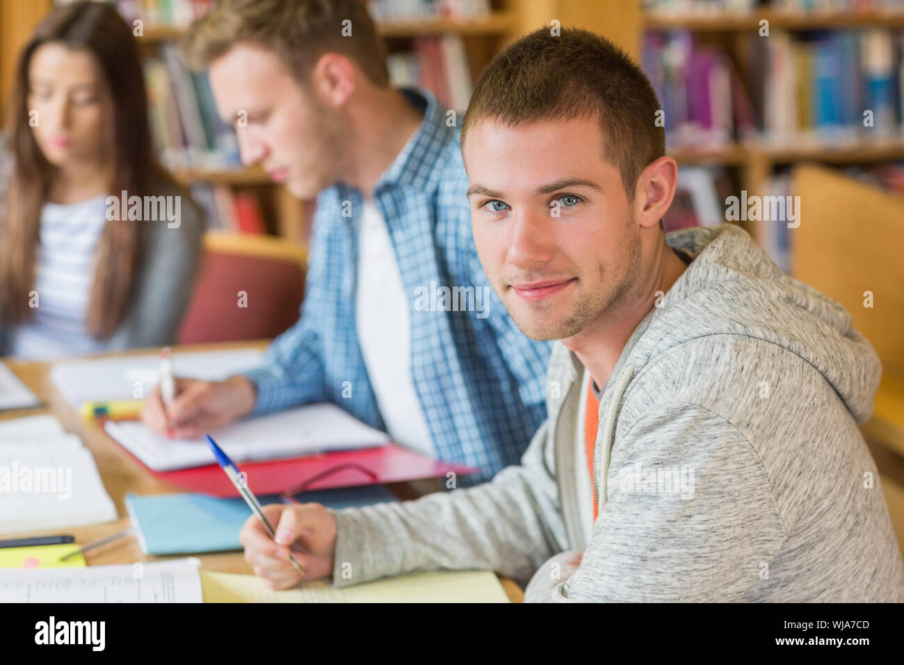 Group portrait of students writing notes at desk in the college library ...