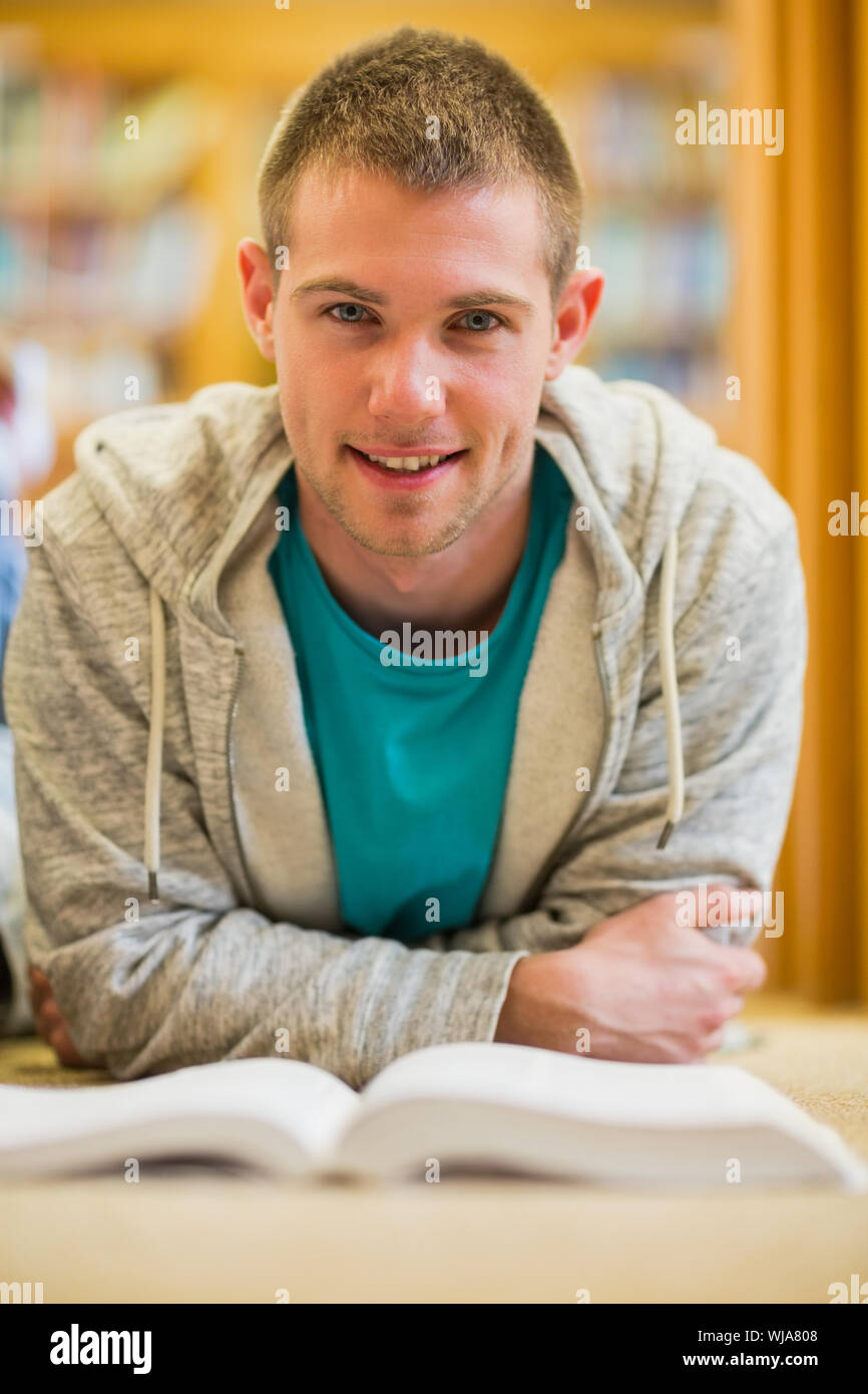 Portrait of a smiling male student with book on the college library ...
