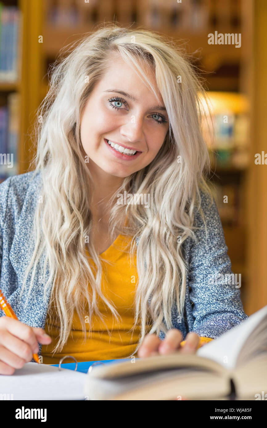 Portrait of a smiling female student sitting at desk in the college ...