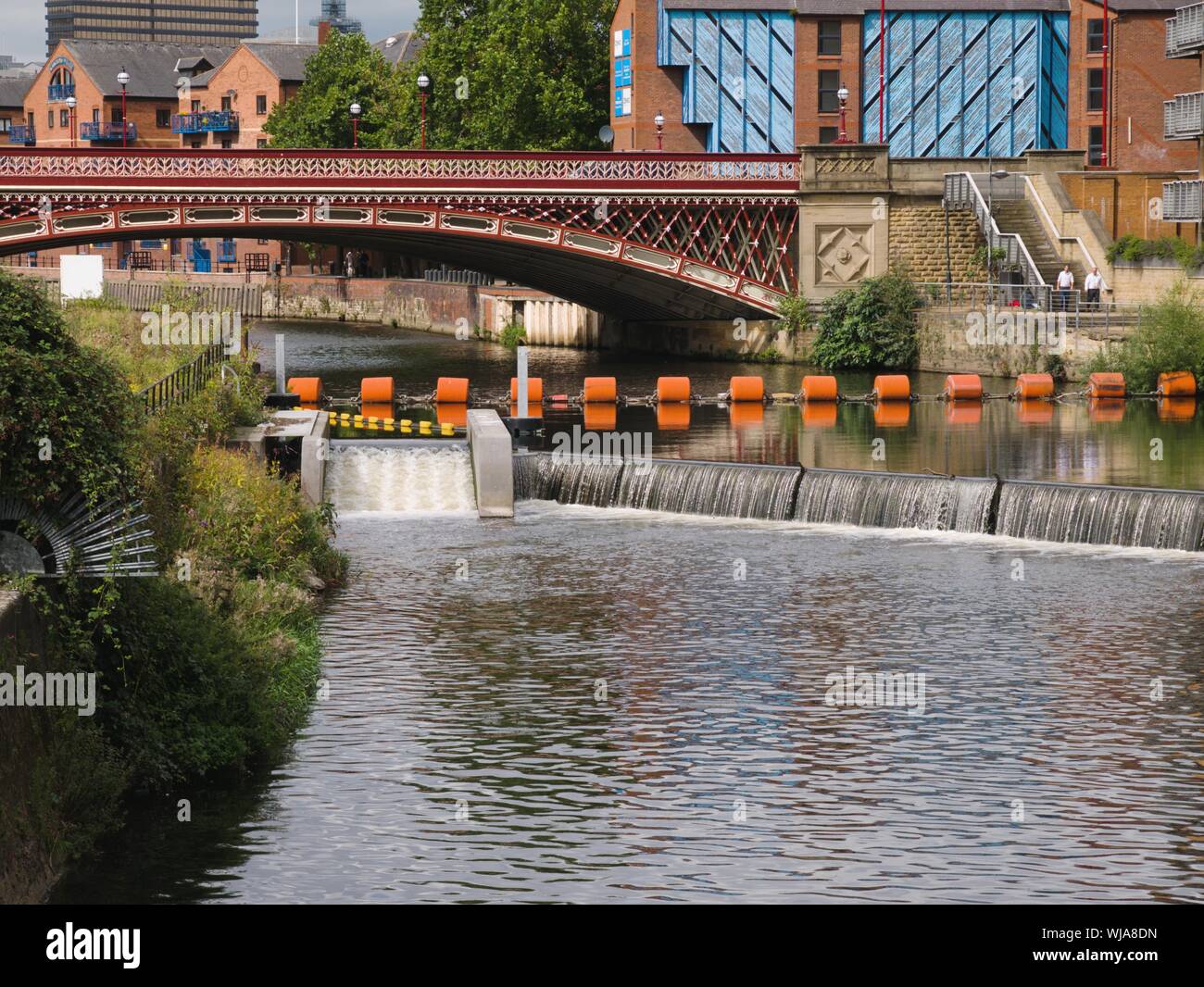 River aire flowing through Leeds with bridge weir orange boom and over ...