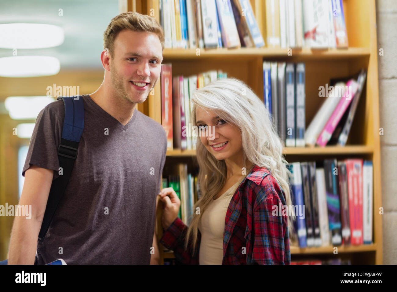 Portrait of a smiling young couple against bookshelf in the library ...