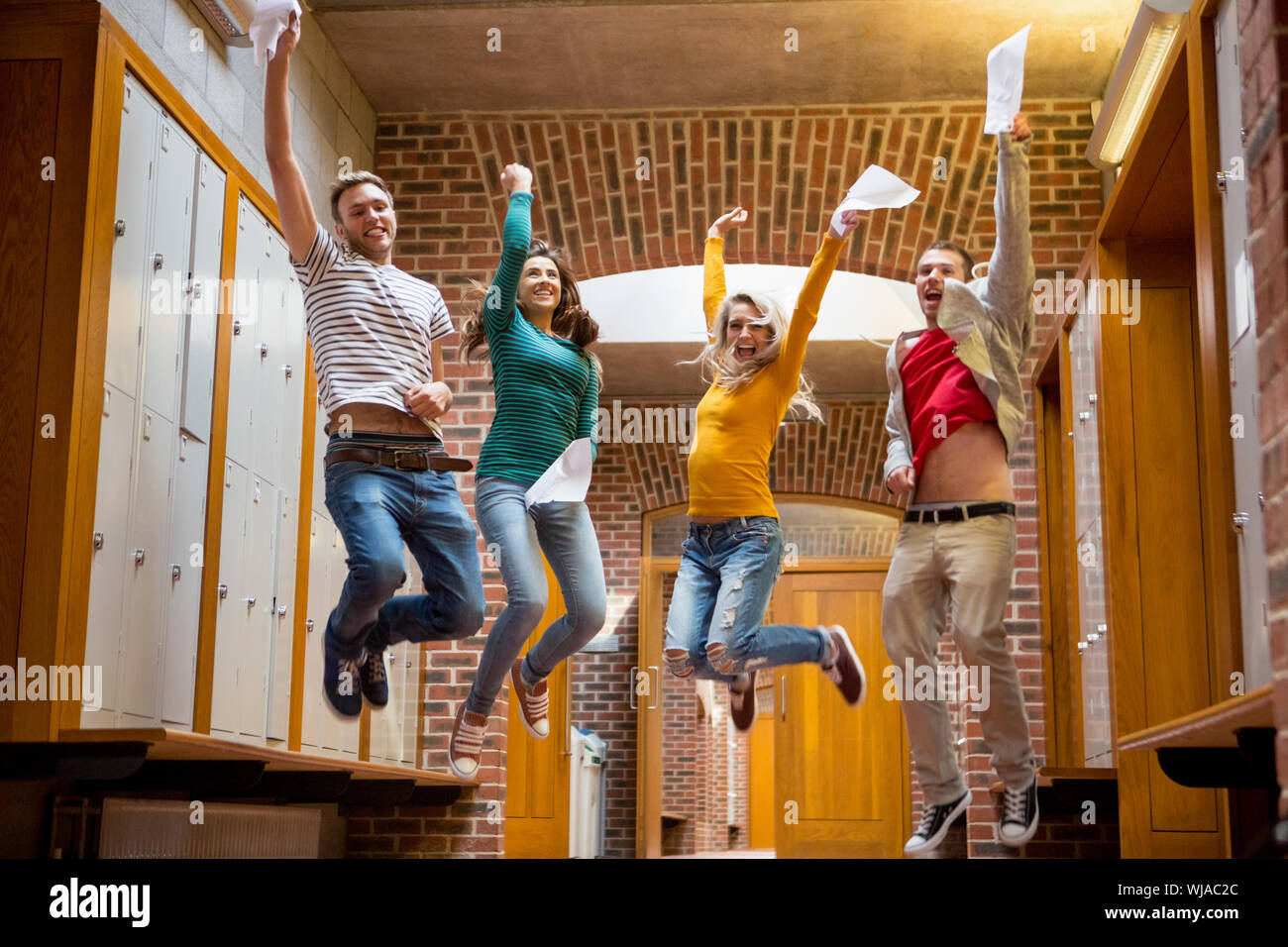 Full length of a group of students jumping in college corridor Stock ...