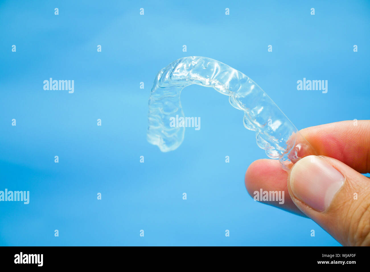 hand holding clear plastic retainer teeth that isolated on blue sky ...