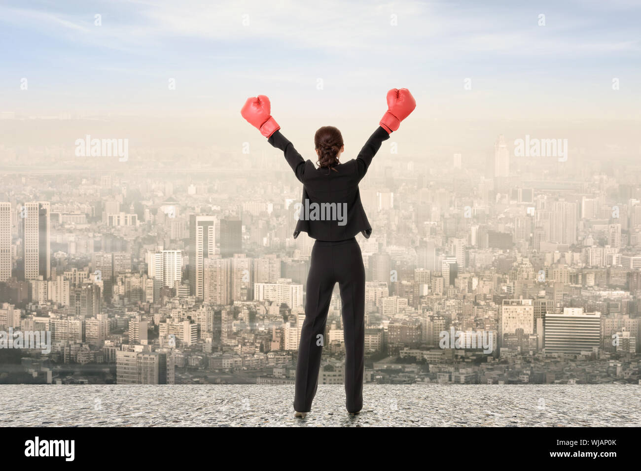 Rear view of business woman raising arms with boxing glove, full length ...