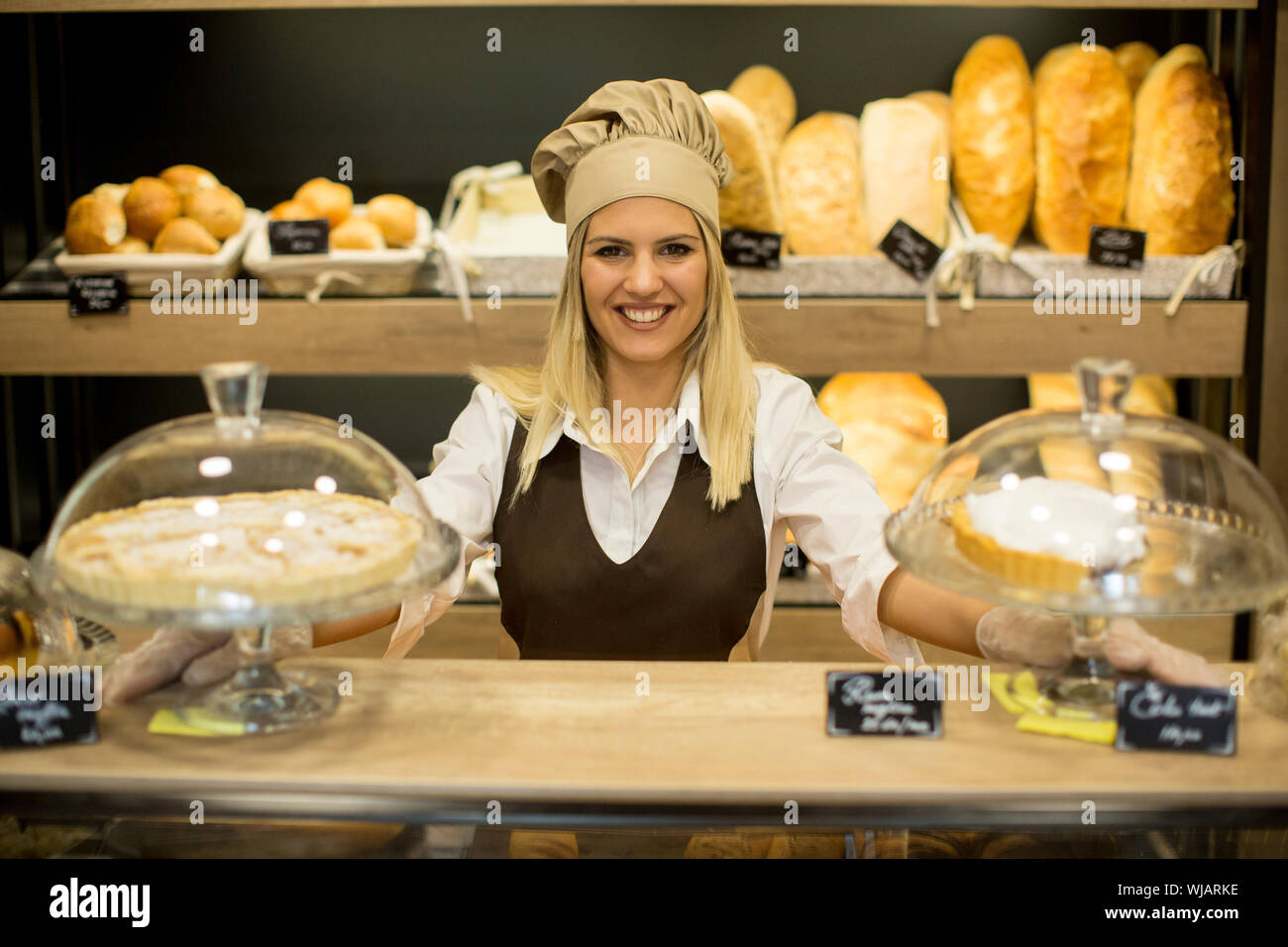 Portrait of friendly female baker with fresh bread smiling in bakery ...