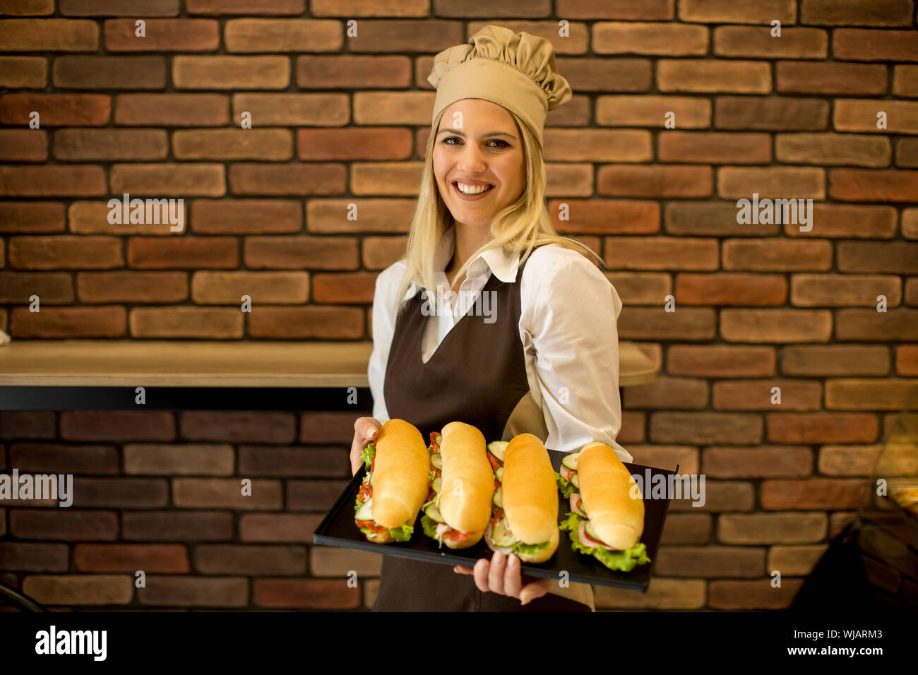 Portrait of female baker posing with various types of sandwiches in the ...