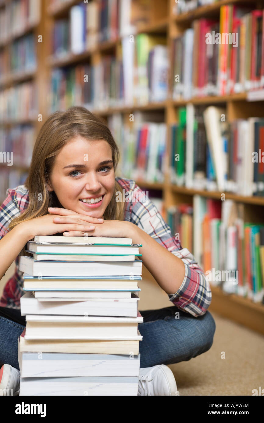 Happy student sitting on library floor leaning on pile of books Stock ...