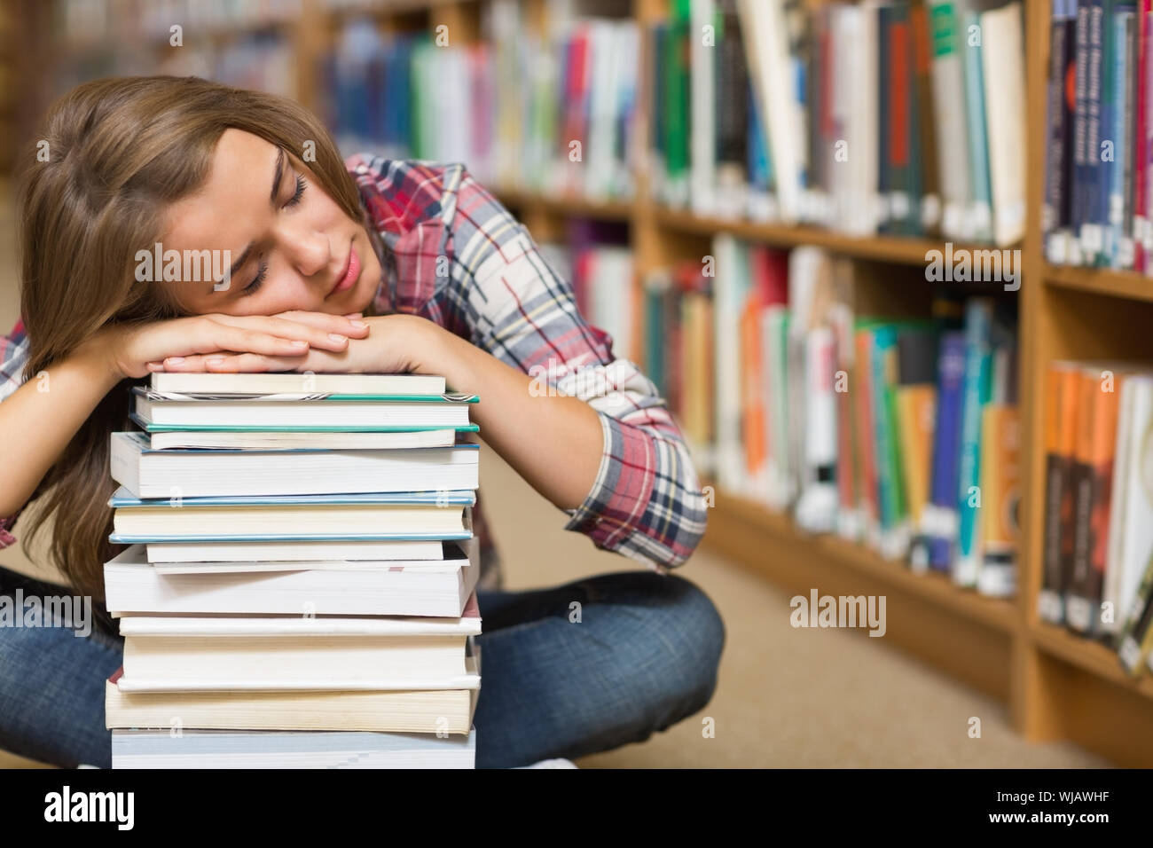 Sleeping student sitting on library floor leaning on pile of books ...