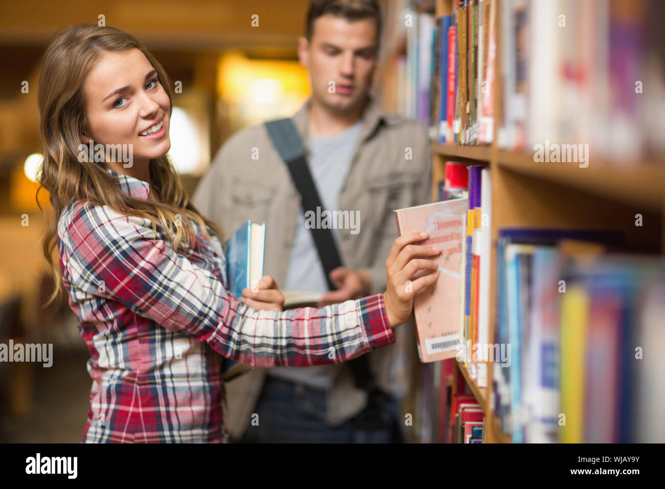 Happy student taking book from shelf in library Stock Photo - Alamy