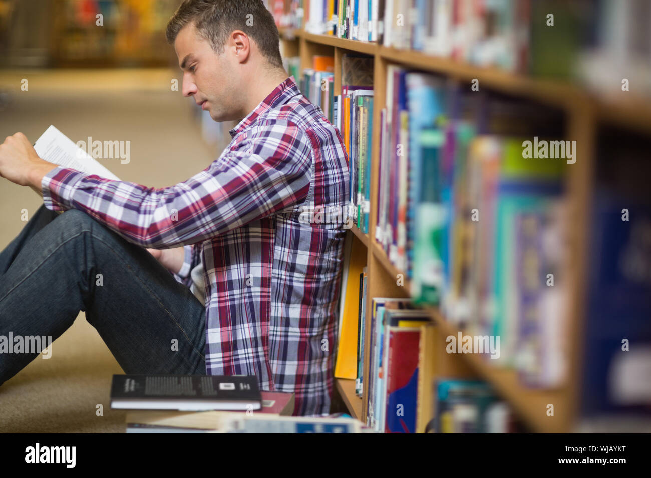 Focused young student sitting on library floor reading Stock Photo - Alamy