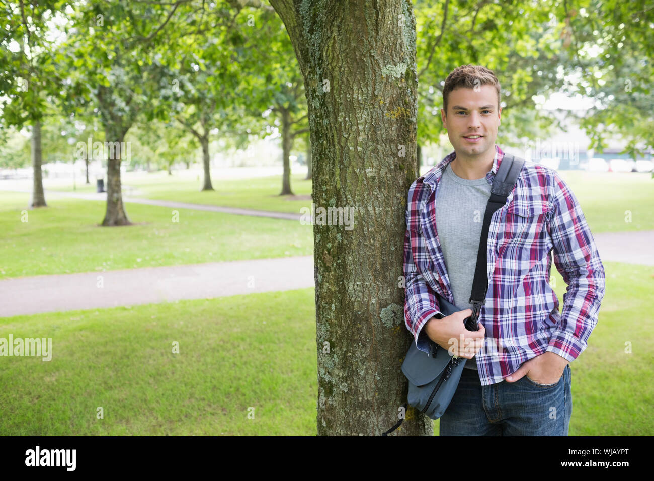 Smiling student leaning on tree holding his digital tablet Stock Photo ...