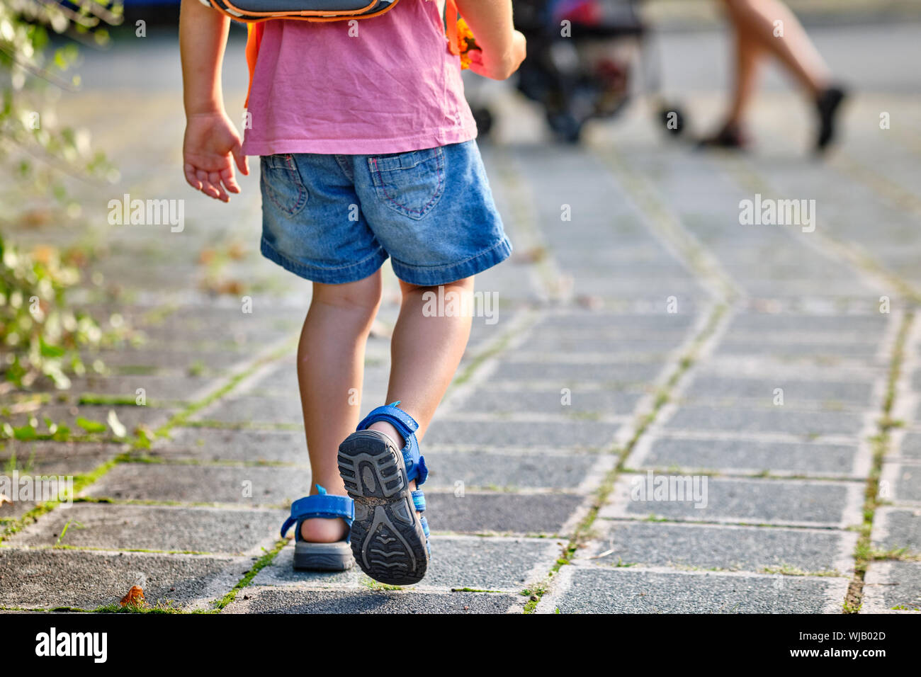 Rear view of a 3-4 year old child walking behind his mother with a ...