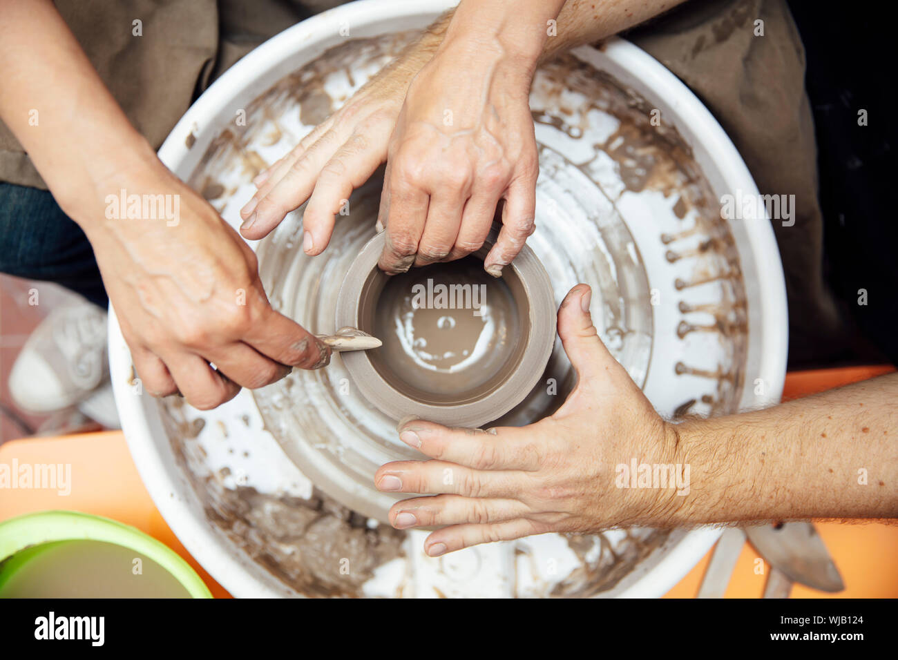 Top view at senior woman spinning clay on a wheel with a help of a ...