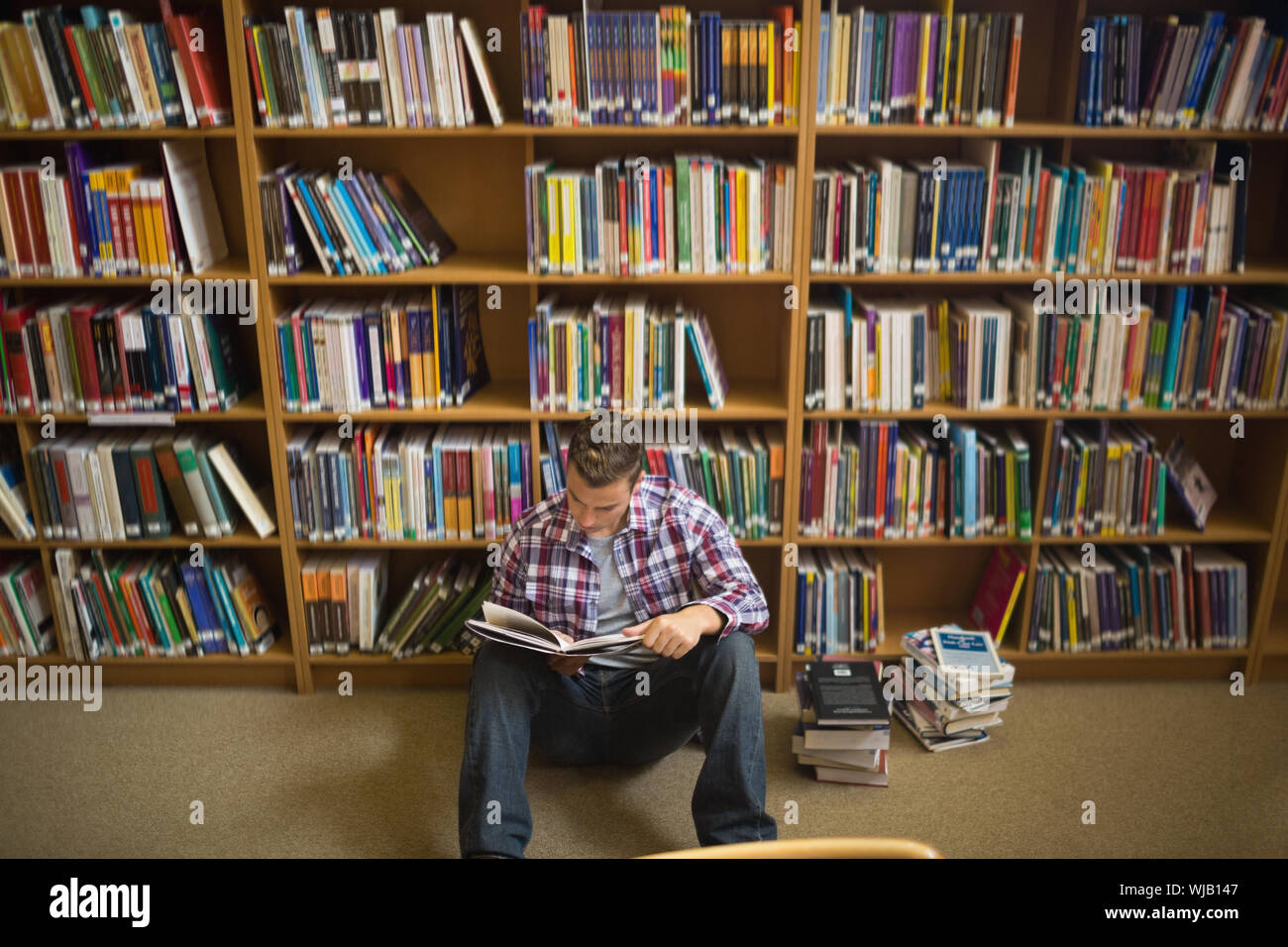 Concentrating young student sitting on library floor reading Stock ...