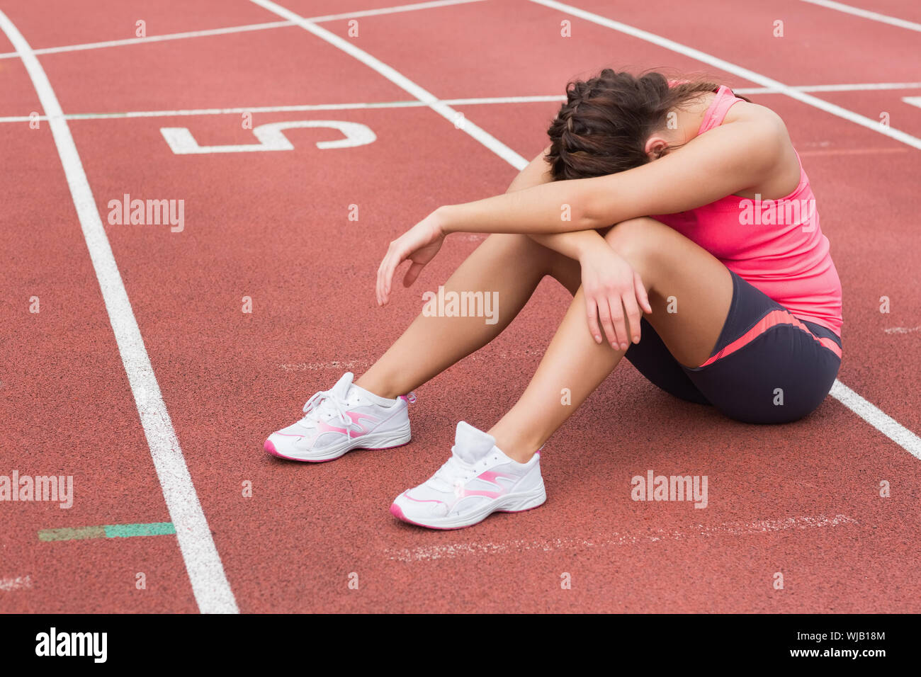 Tensed sporty woman sitting on the running track Stock Photo - Alamy