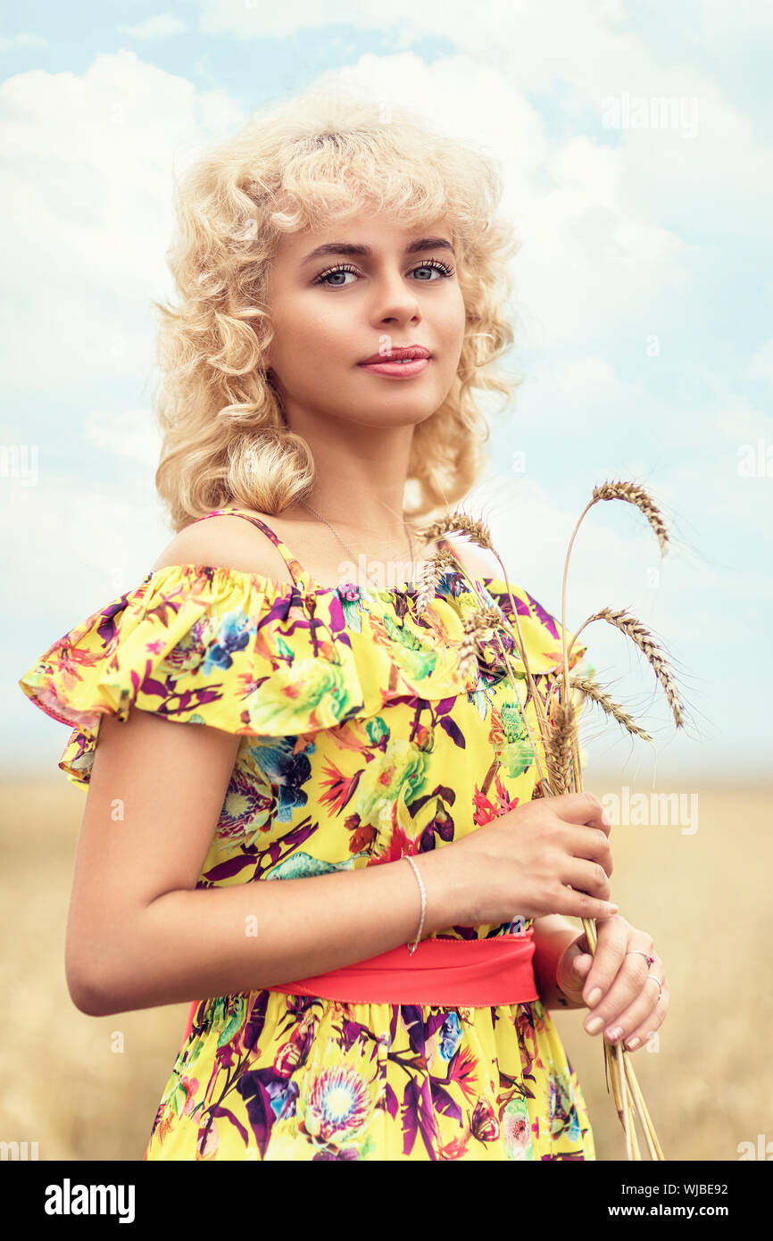 Portrait of a girl with curly blond hair, holding ripe spikelets of ...