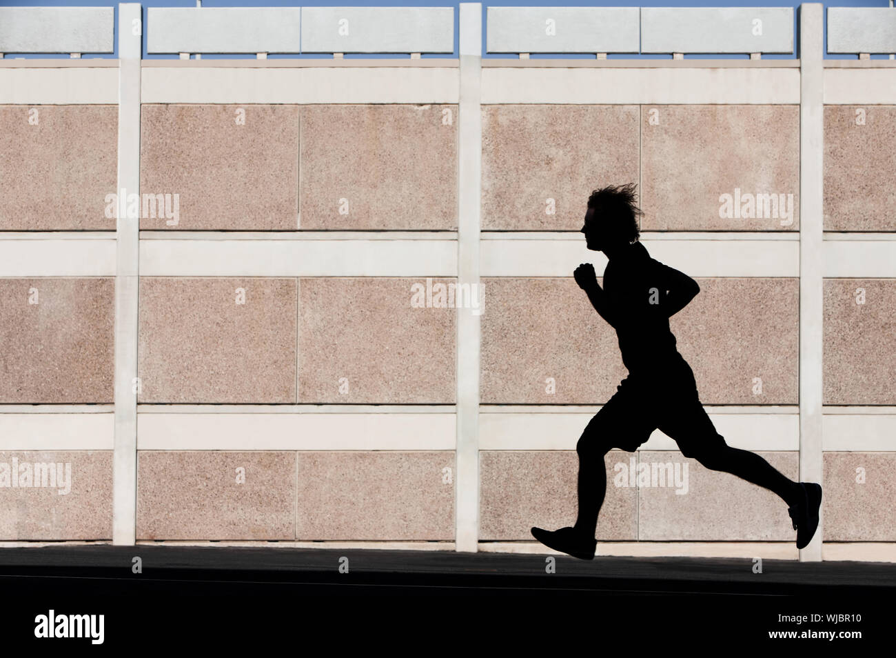 Man in the shadows of building runs for exercise Stock Photo - Alamy