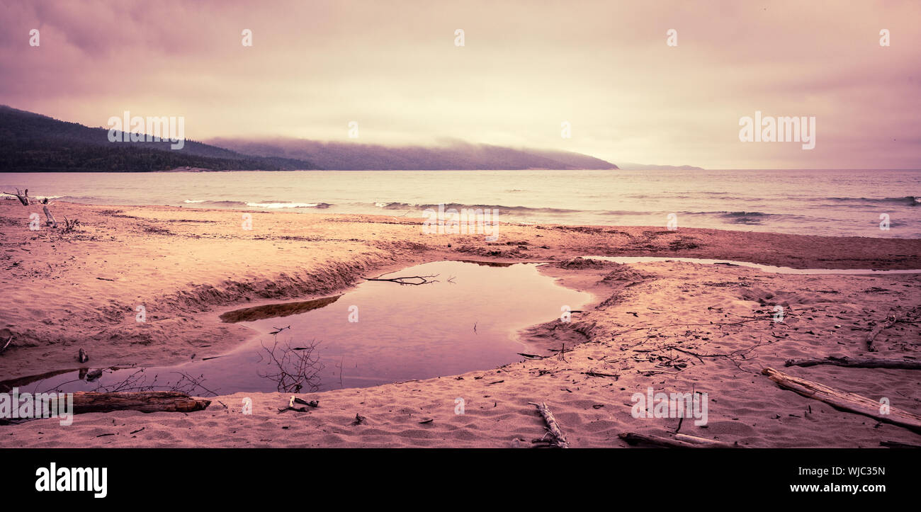 Calm reflective puddle with the stormy waters of lake Superior in the ...
