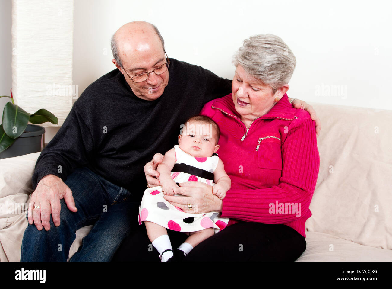 Grandparents holding baby girl on lap while sitting on couch in ...