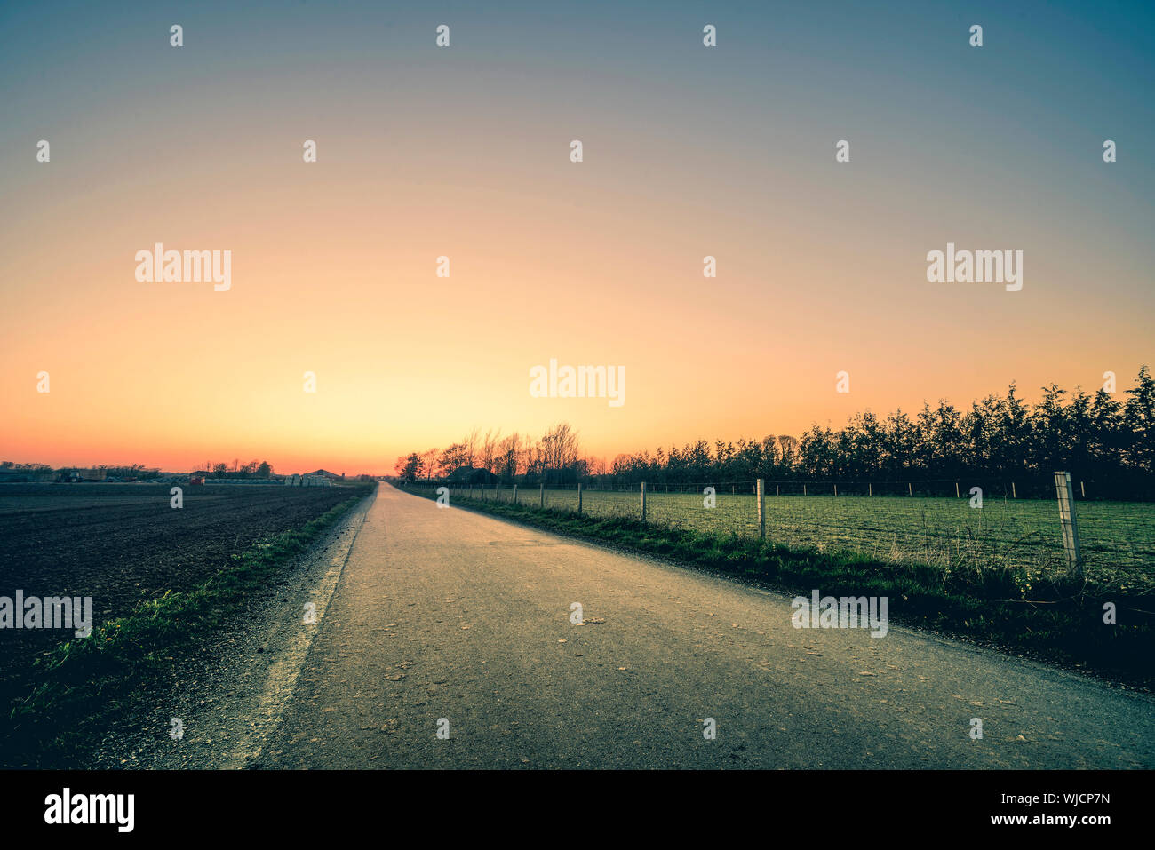 Road to a sunset in a rural environment with a fence on the right side ...