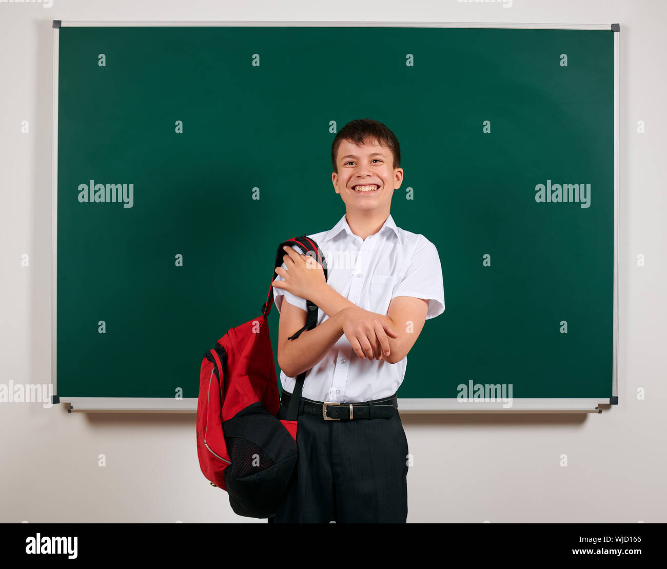 Portrait of a school boy posing with backpack on blackboard background ...