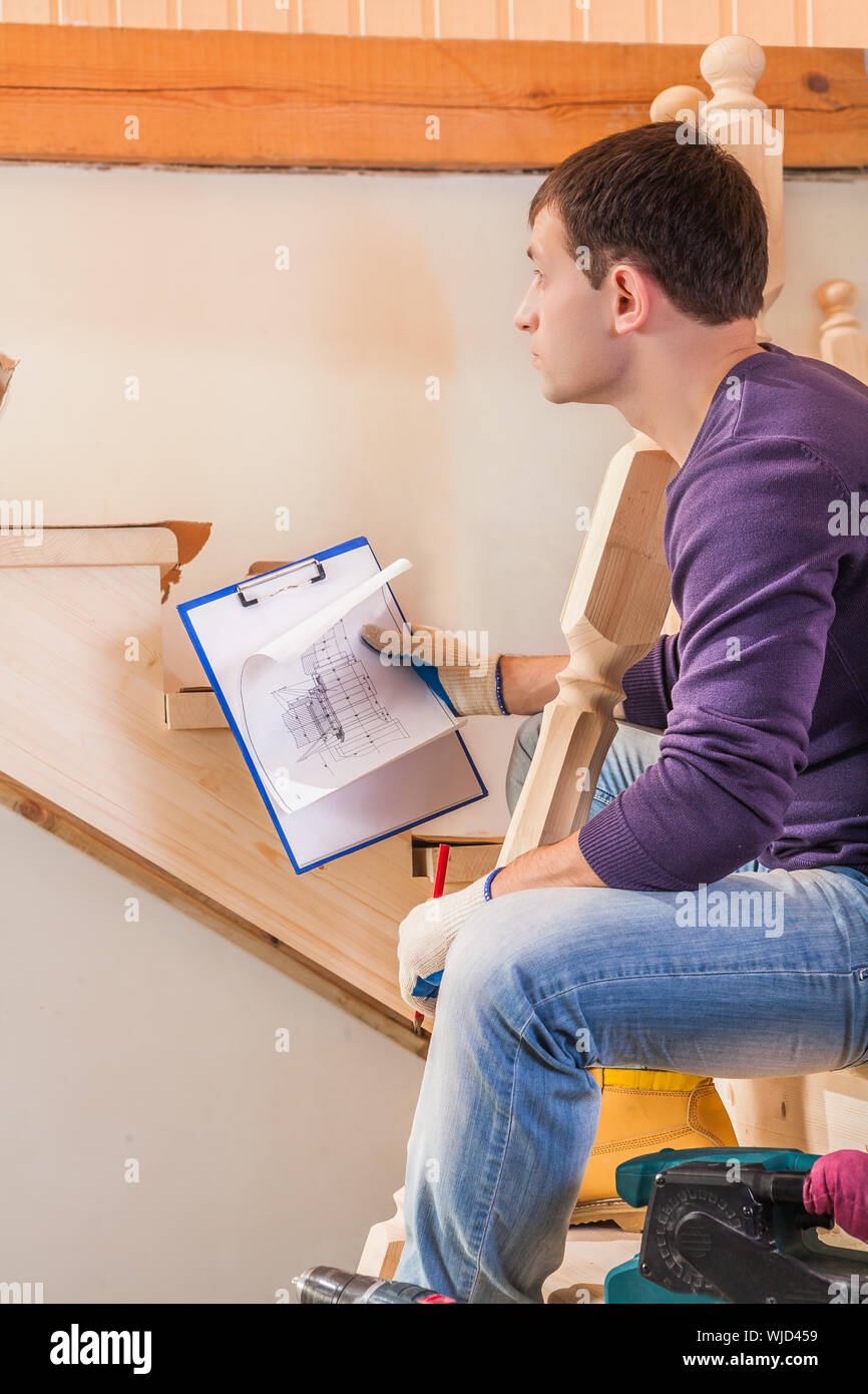 a young carpenter holding blueprint and sitting on ladder Stock Photo ...