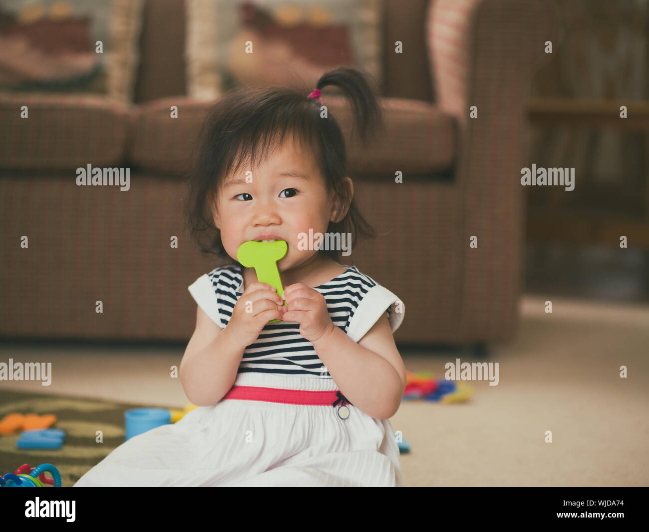 Cute Girl Biting Toy While Sitting At Home Stock Photo - Alamy