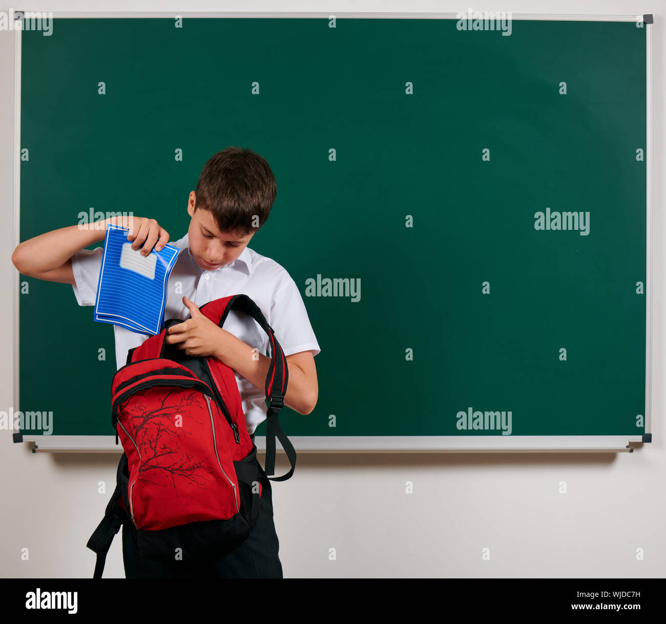 Portrait of a school boy looking for school supplies in his backpack ...