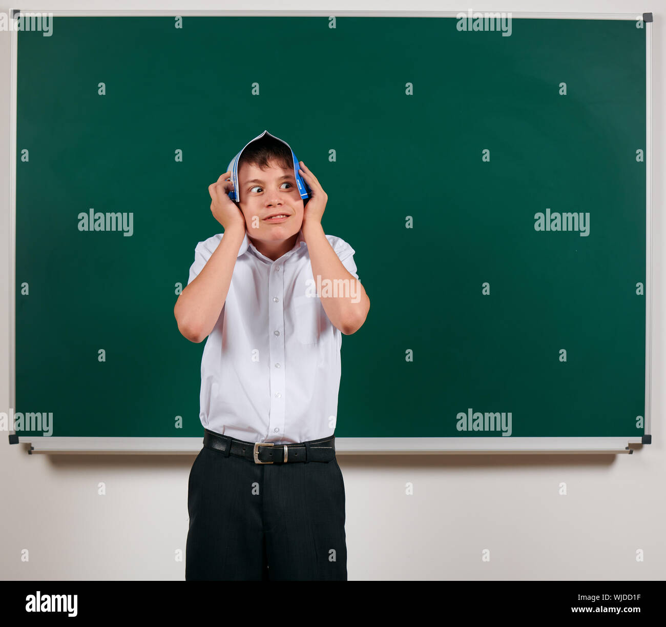 Portrait of a school boy posing with blue exercise book on blackboard ...