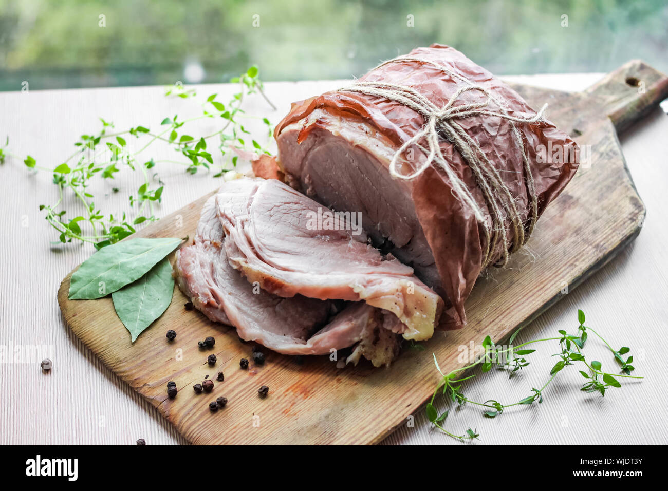 Homemade baked pork ham on rustic cutting board with aromatic herbs ...