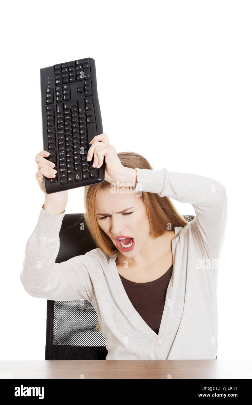 Beautiful casual woman behind the desk trying to broke the keyboard ...