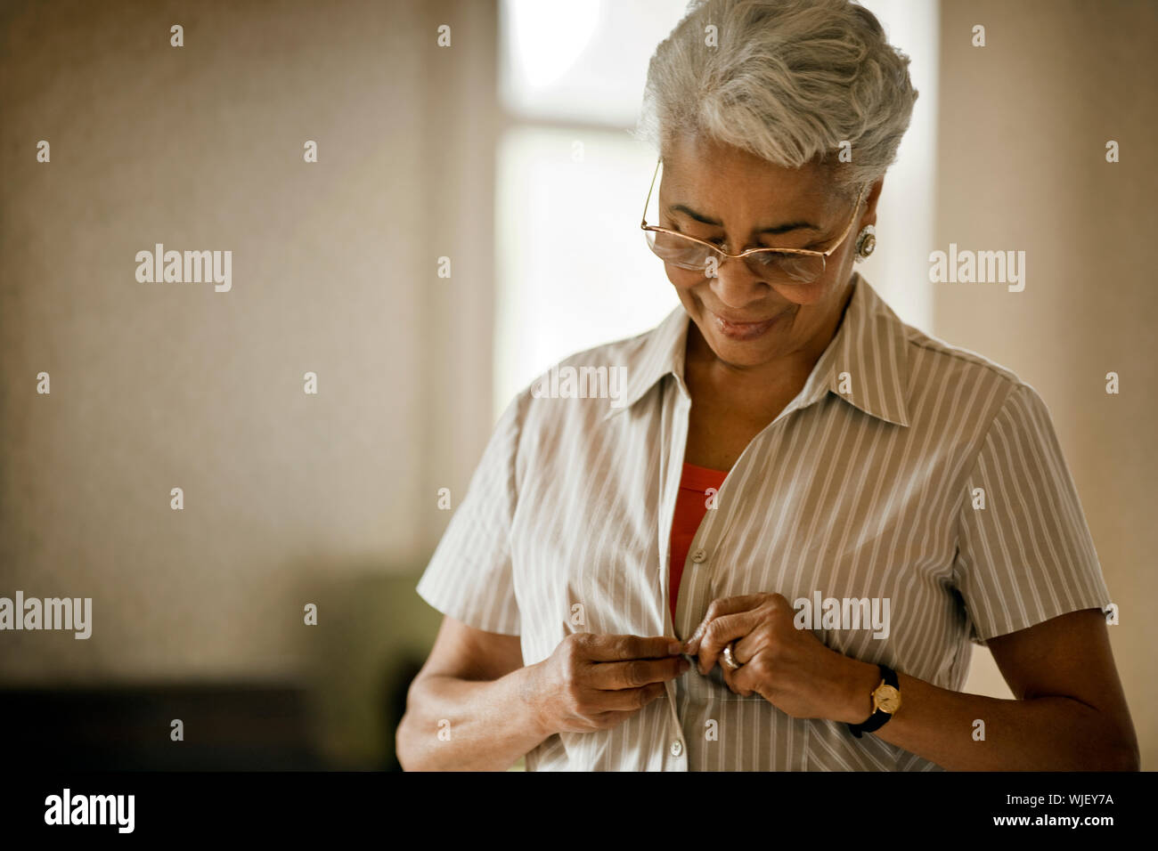 Woman looking down as she buttons up her shirt Stock Photo - Alamy