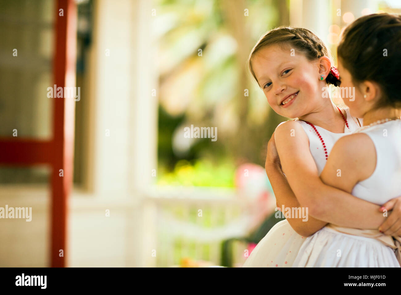 Young girl in party dress smiles while hugging another girl as she ...