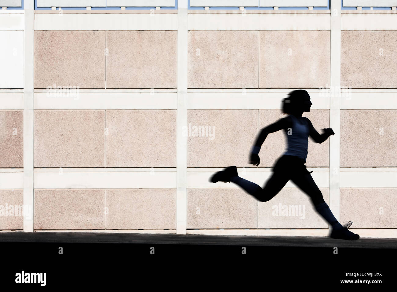 Woman in the shadows of building runs for exercise Stock Photo - Alamy