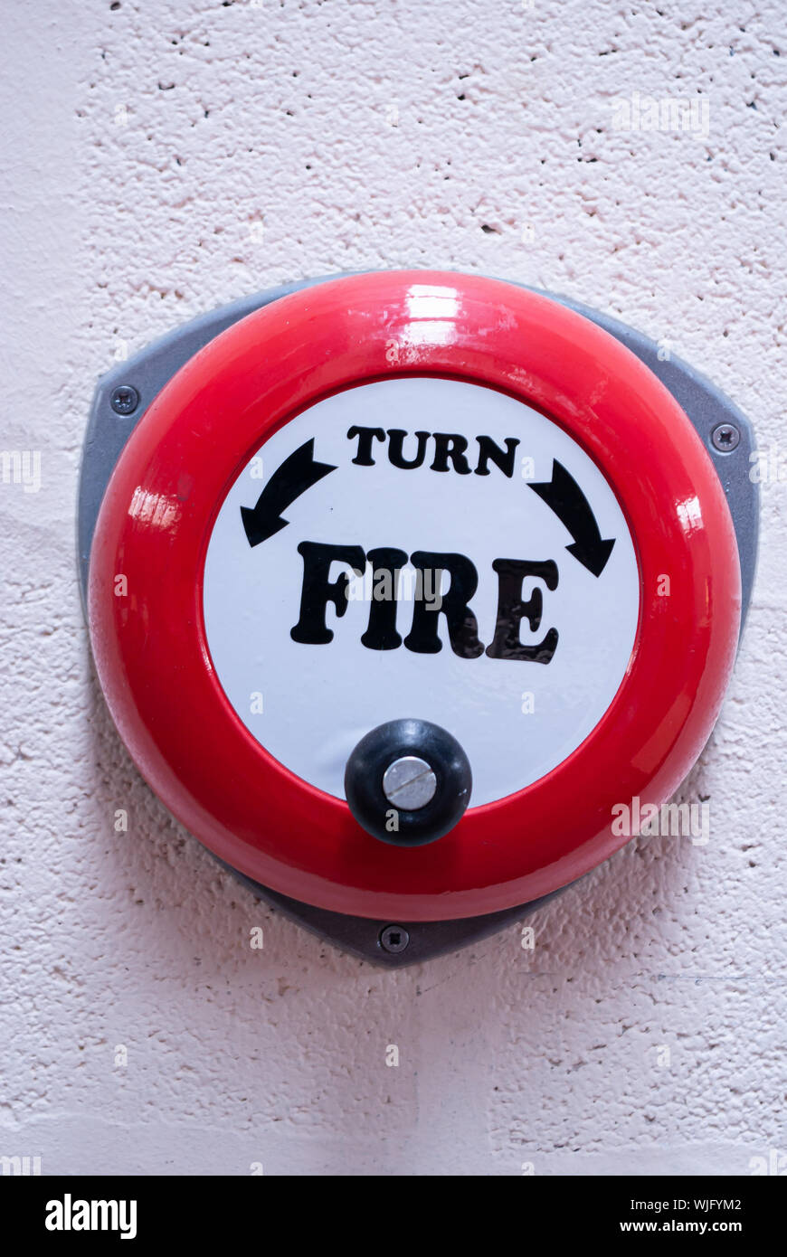 Red manual-turning fire bell on a white breeze-block wall (Portrait ...