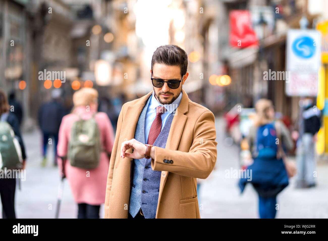 A handsome elegant man walking on the streets and checking the time on ...