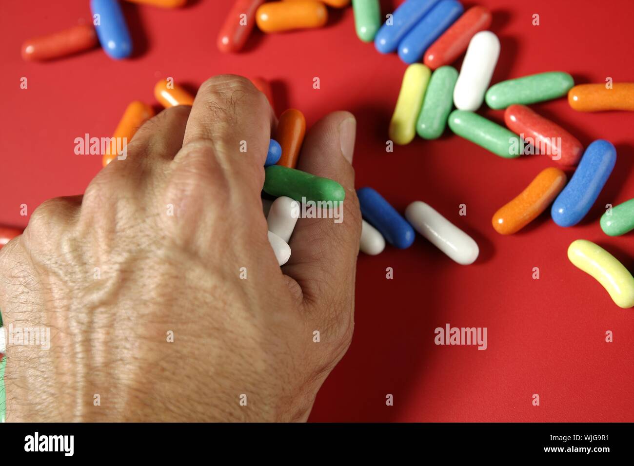 Human man hand holding colorful candy sweets over red Stock Photo - Alamy