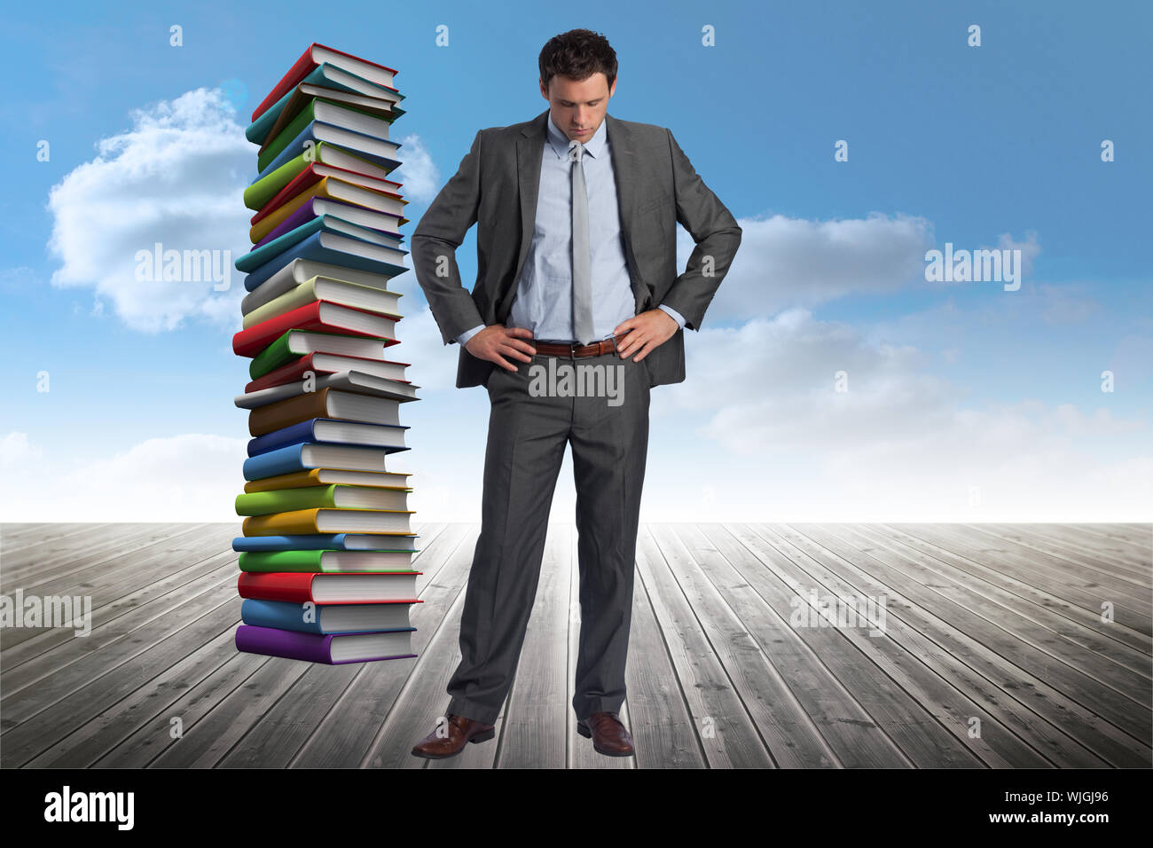 Serious businessman with hands on hips against stack of books against ...