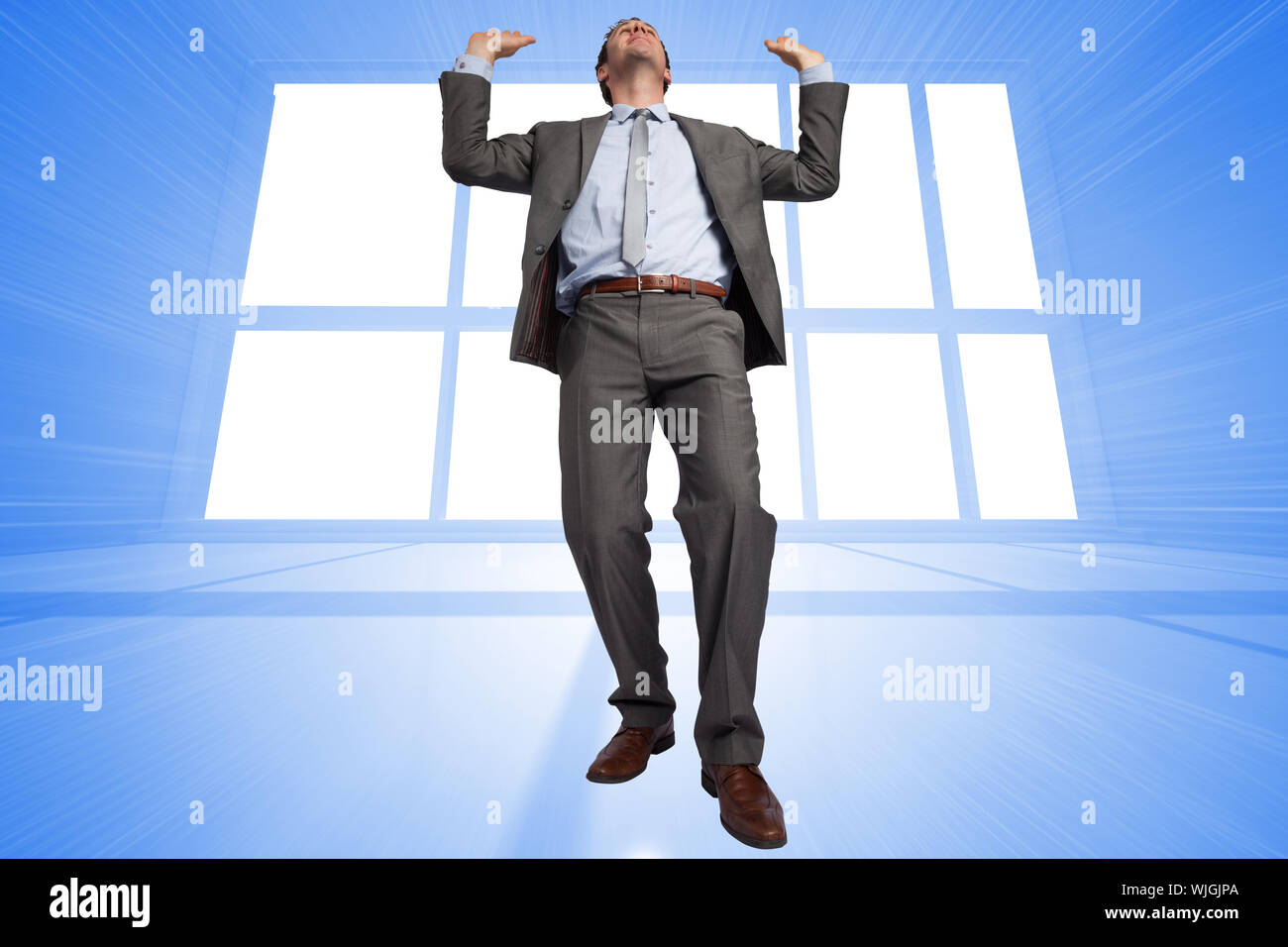 Businessman posing with hands up against bright blue room with windows ...