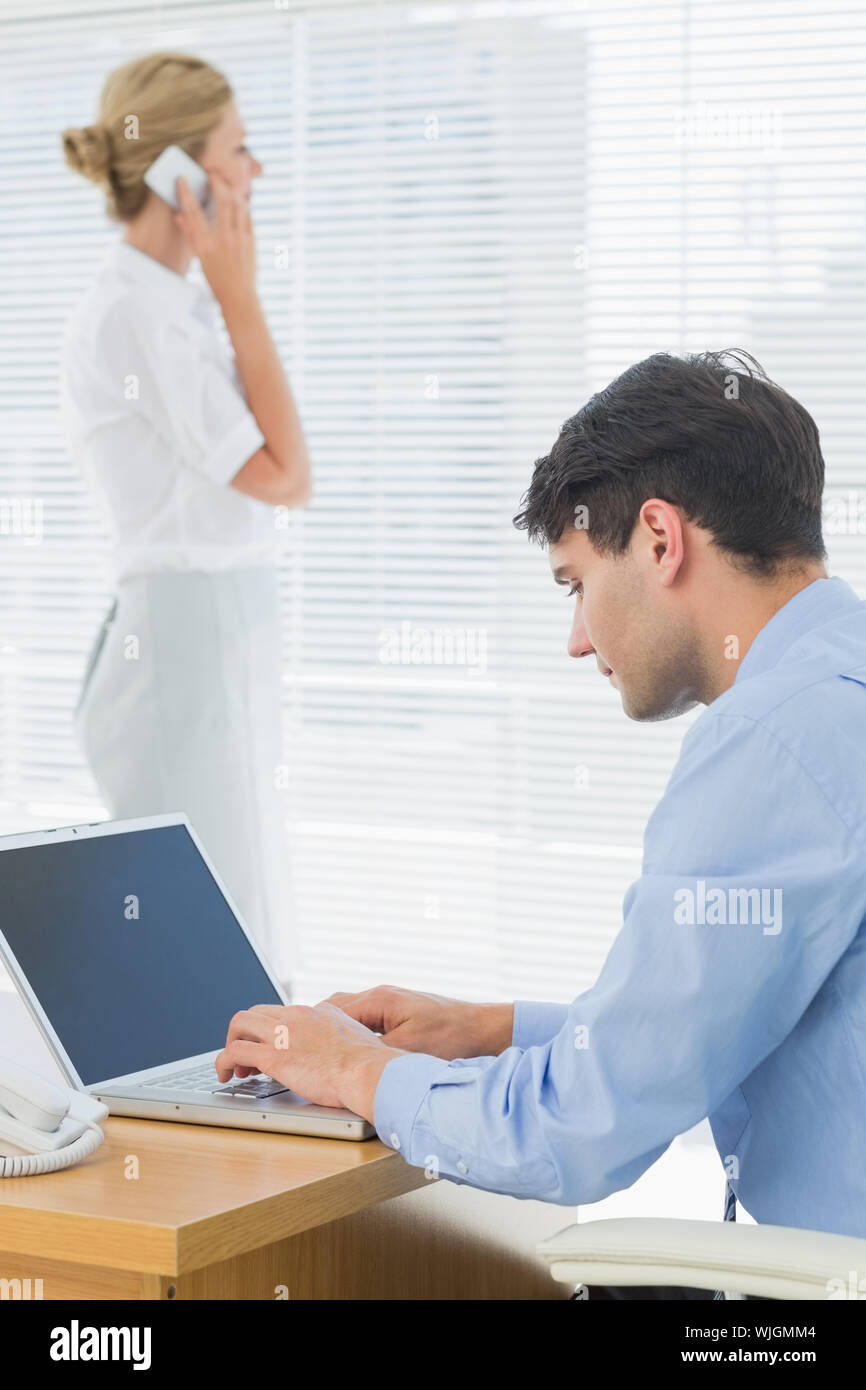 Side view of a young businesswoman using cellphone while man working on ...