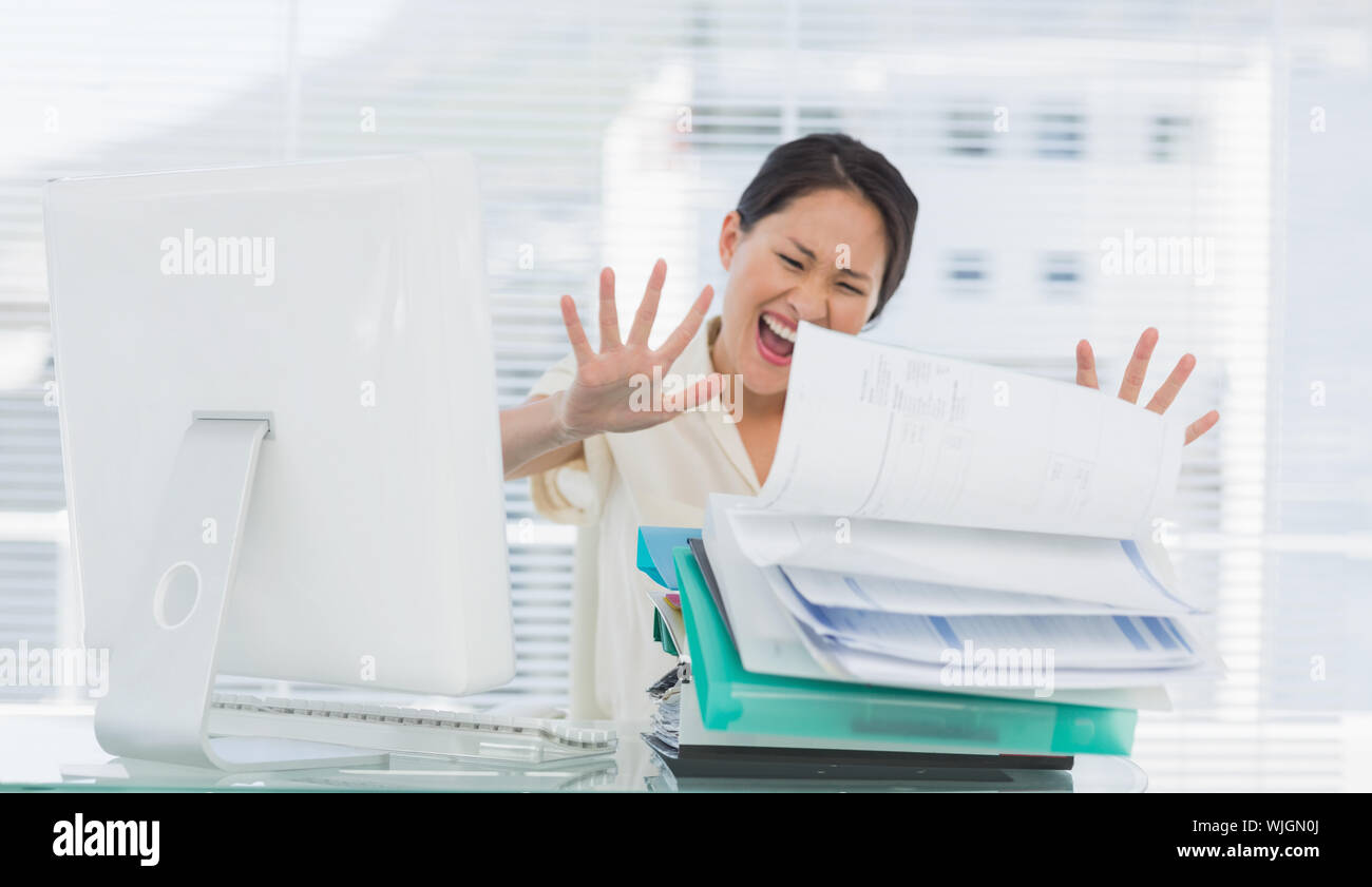 Angry young businesswoman shouting with stack of folders at office desk ...